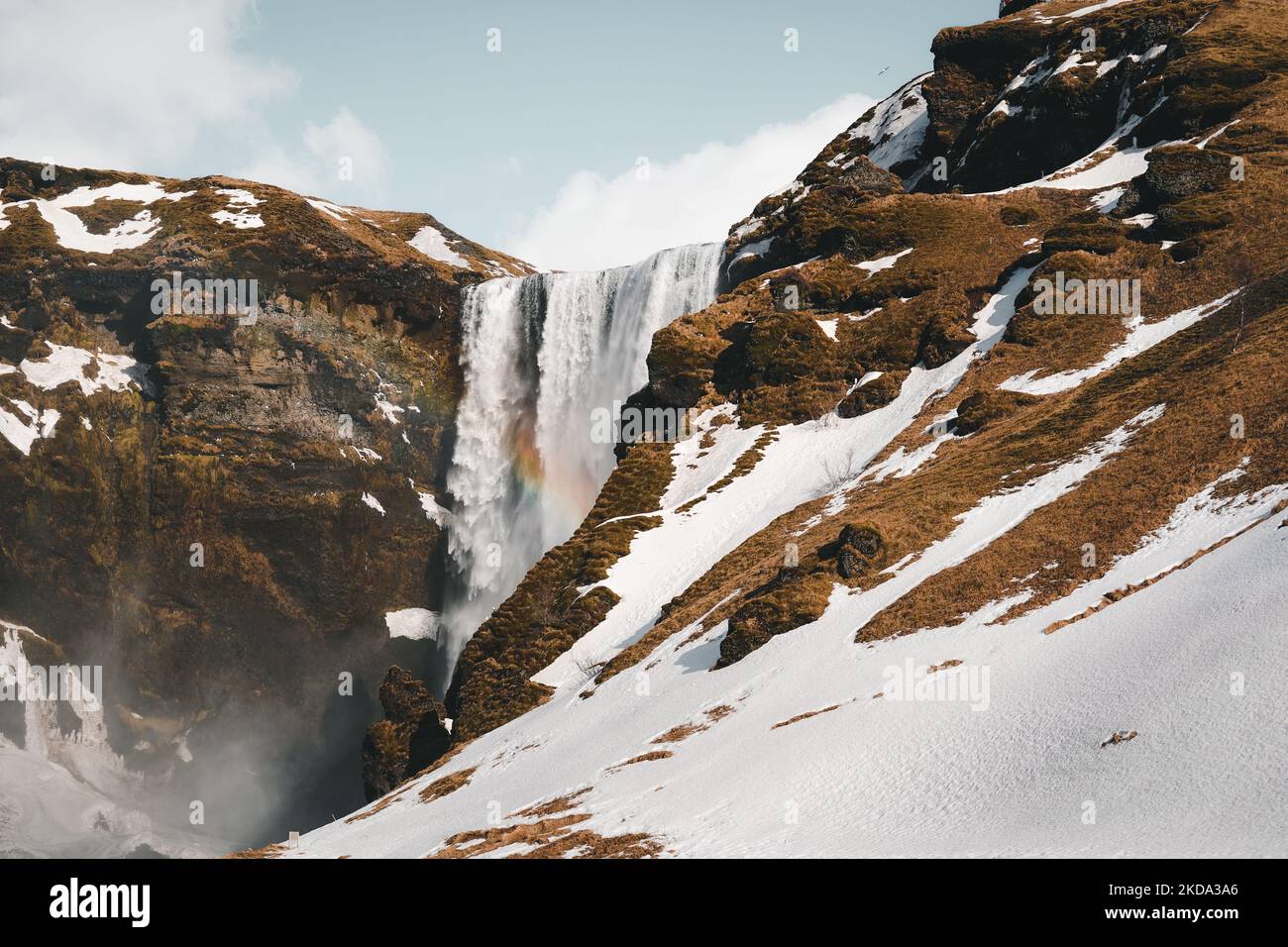 An aerial view of flowing waterfall surrounded by snow covered cliffs ...