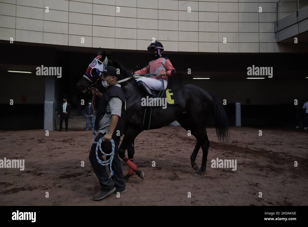 Caretakers and trainers assist jockeys and horses in the oval area ...