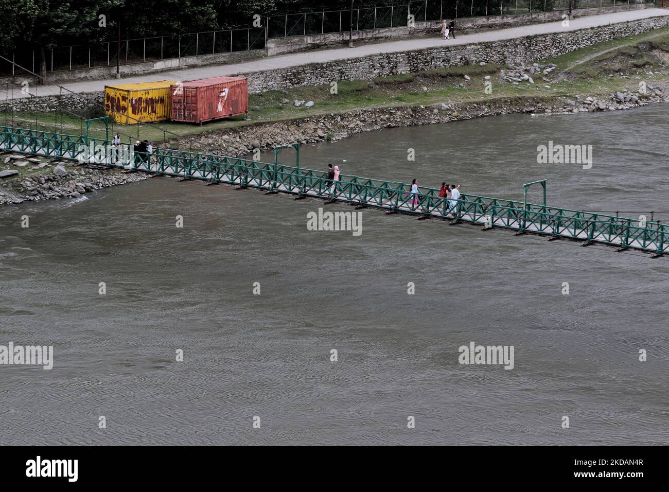 People walk over a wooden partially damaged bridge during gusty winds ...