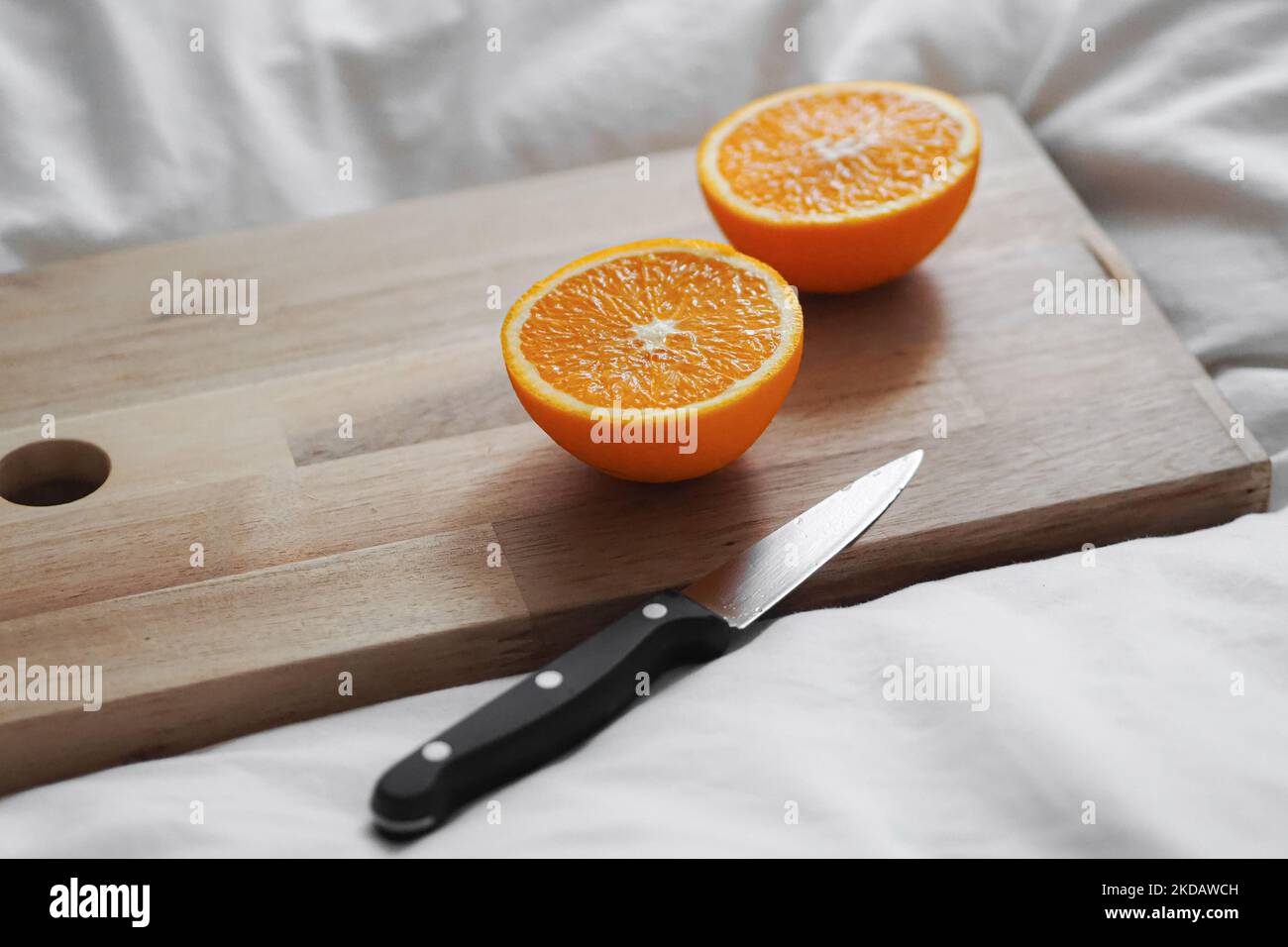 A selective focus of an orange cut in half with black knife on a wooden ...