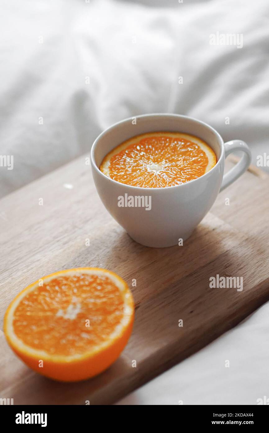 A vertical shot of a tea cup with a sliced orange in it next to a half ...