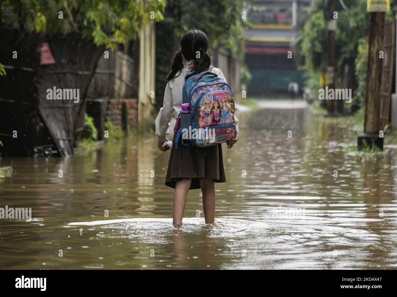 A girl returns from school wades across a flooded street after heavy ...