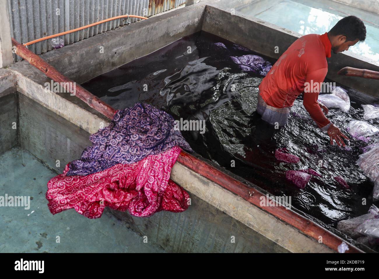 A worker dries fabrics after applying colour at a dye factory in ...