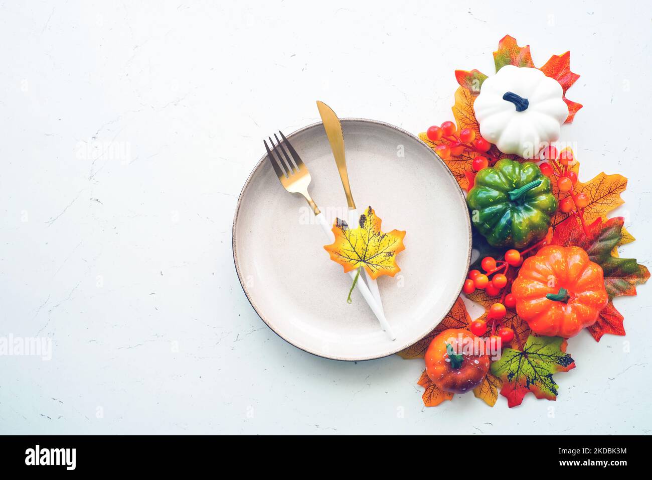 Autumn table setting. White plate, golden cutlery and fall decorations ...