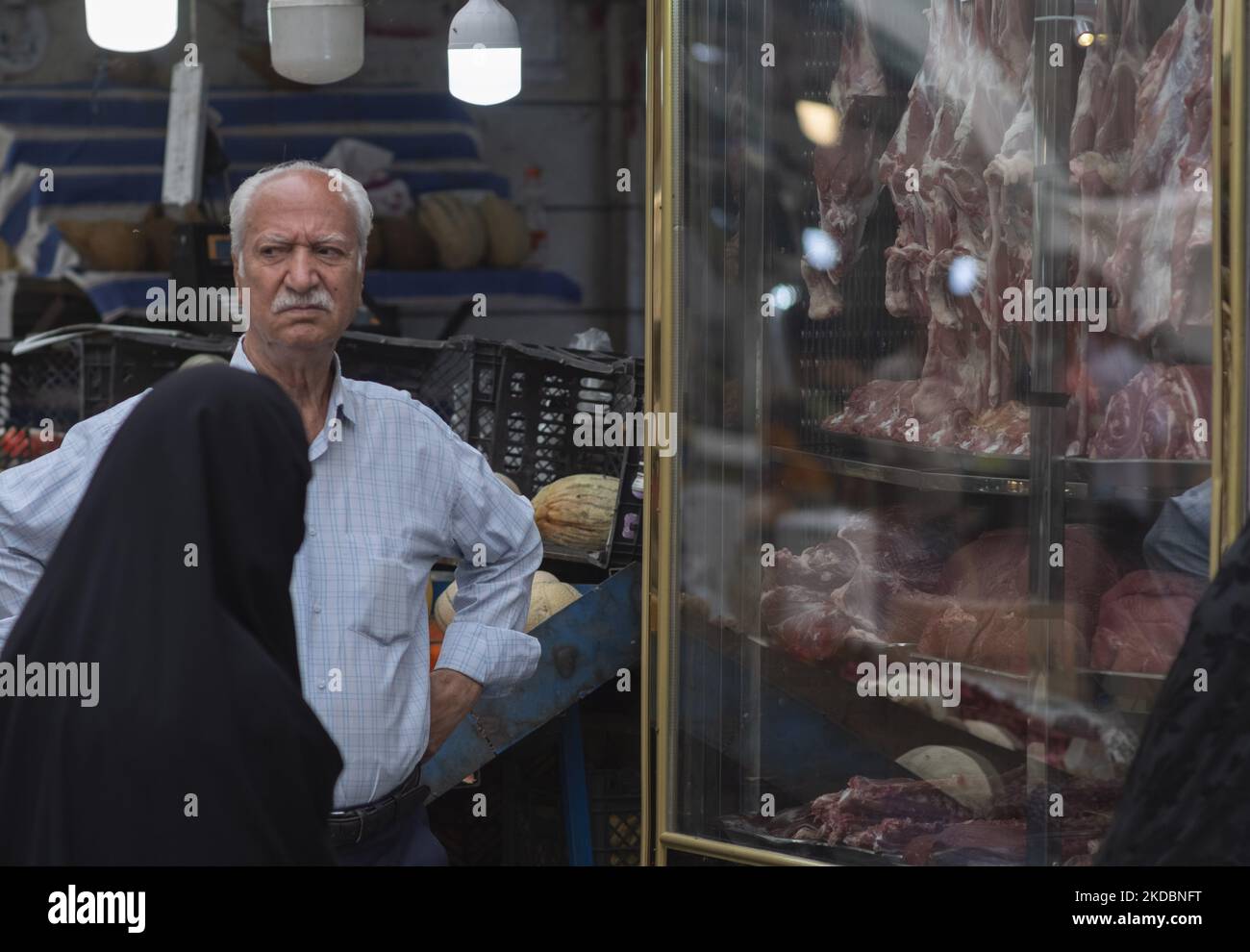 An Iranian elderly man looks on while standing next to a butcher shop ...
