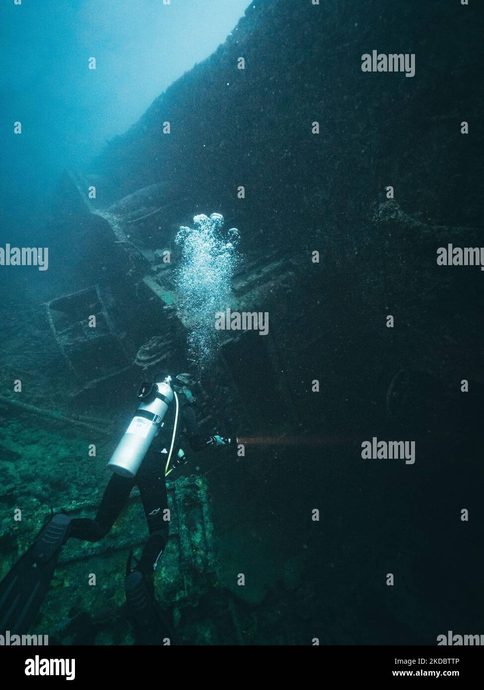 A scuba diver exploring the mysterious ship wrecks, in a vertical shot ...