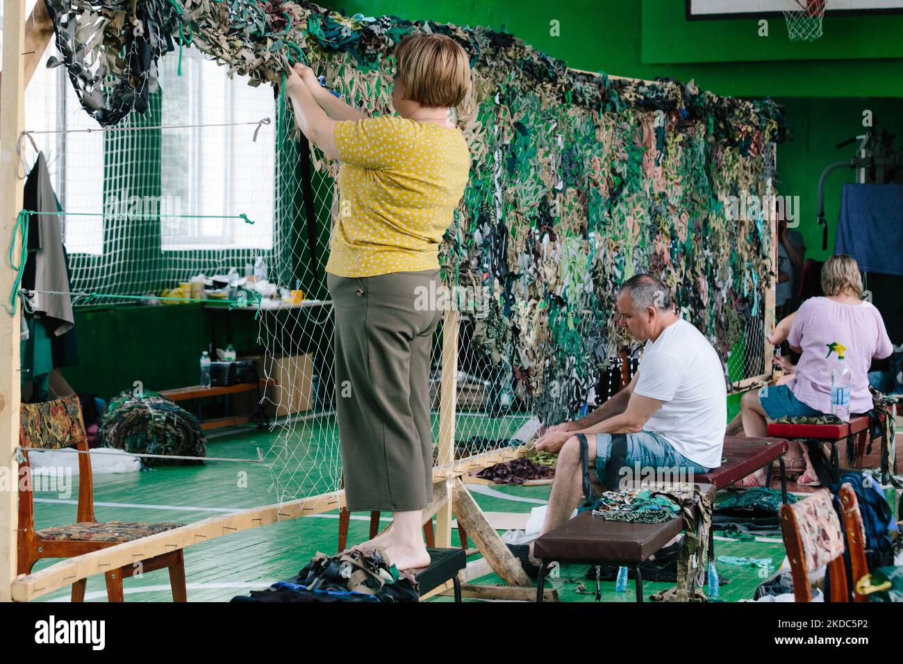 Volunteers weave a camouflage net from old fabrics in the local school ...
