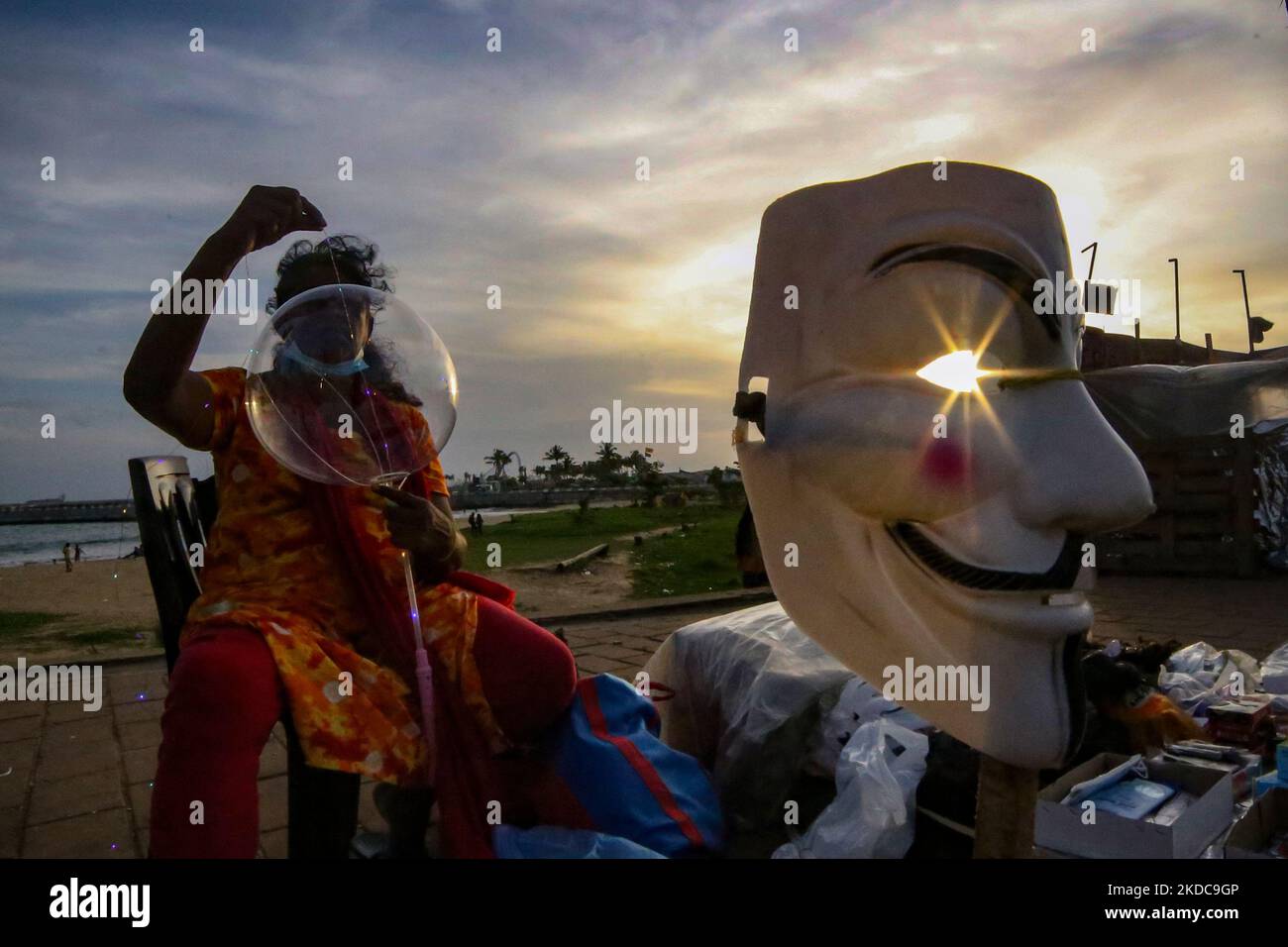 A Sri Lankan street vendor prepares balloons as sun set is seen through ...