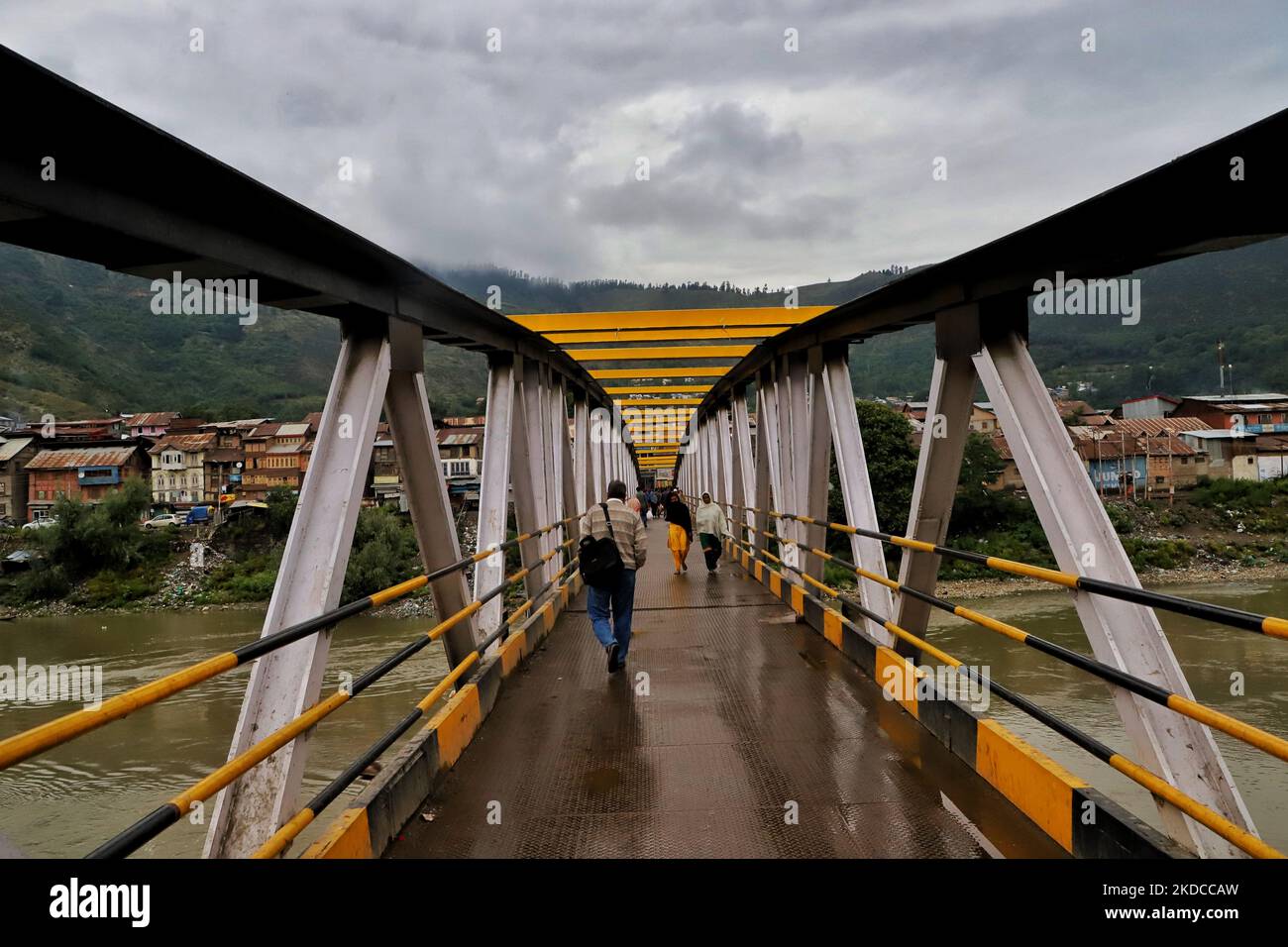 People walk over a bridge as residential houses are seen on the banks ...