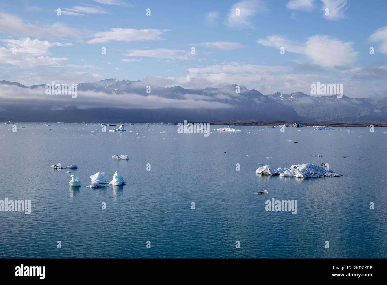 The Jokulsarlon glacial lake with floating ice caps and white clouds in ...
