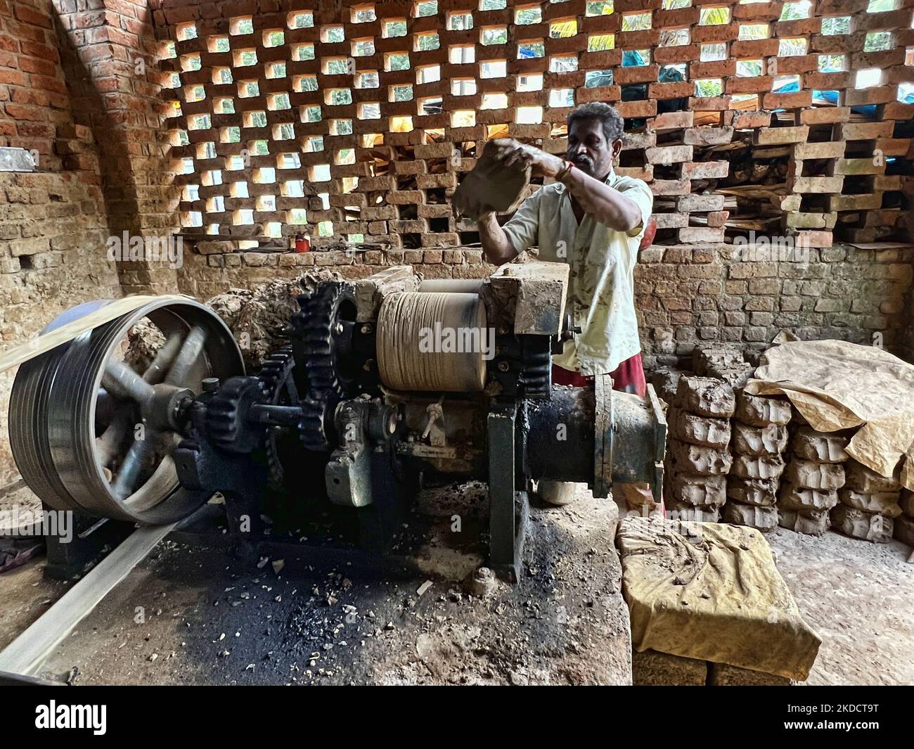 Man places raw clay into a large machine to prepare it before it is ...