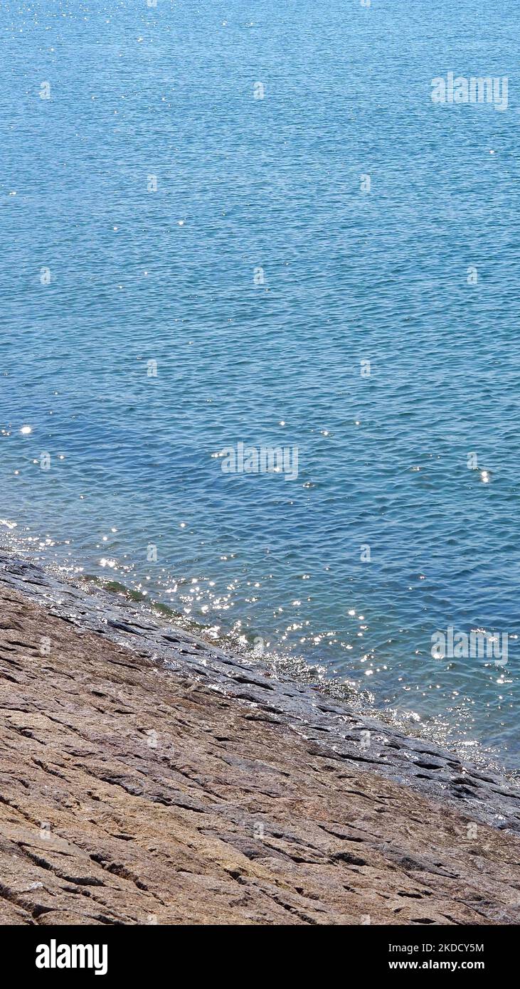 A vertical closeup of a sandy beach with sunlit, shining water waves ...