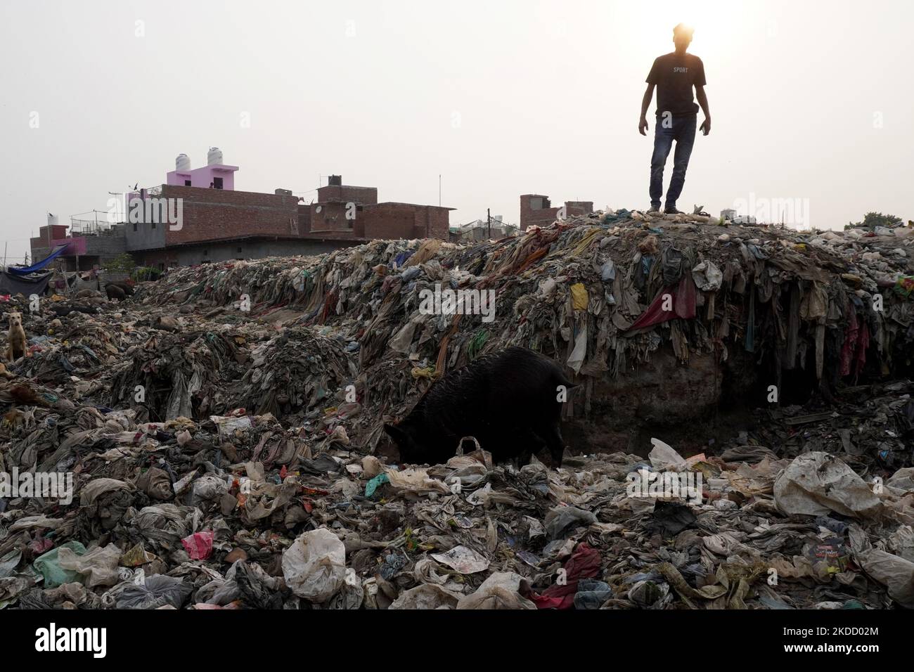 A man stands on top of a pile of garbage along an open drain filled ...
