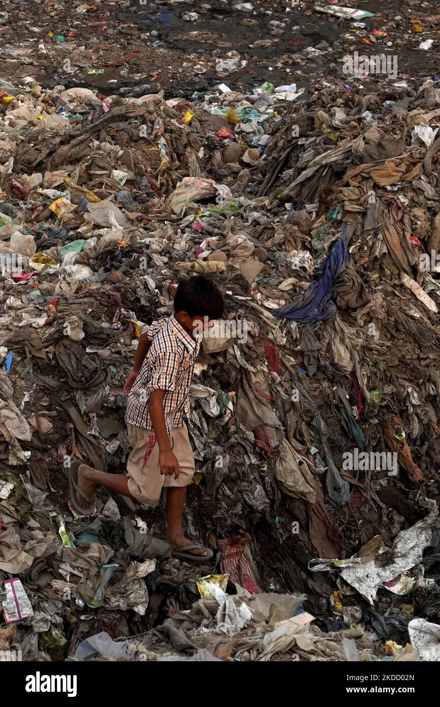 A boy walks amidst a pile of garbage along an open drain filled with ...