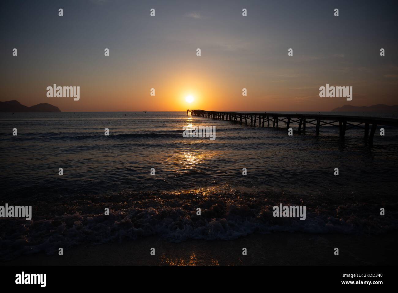 A low focus of the sun during the sunset on a beach, and a sea dock in ...