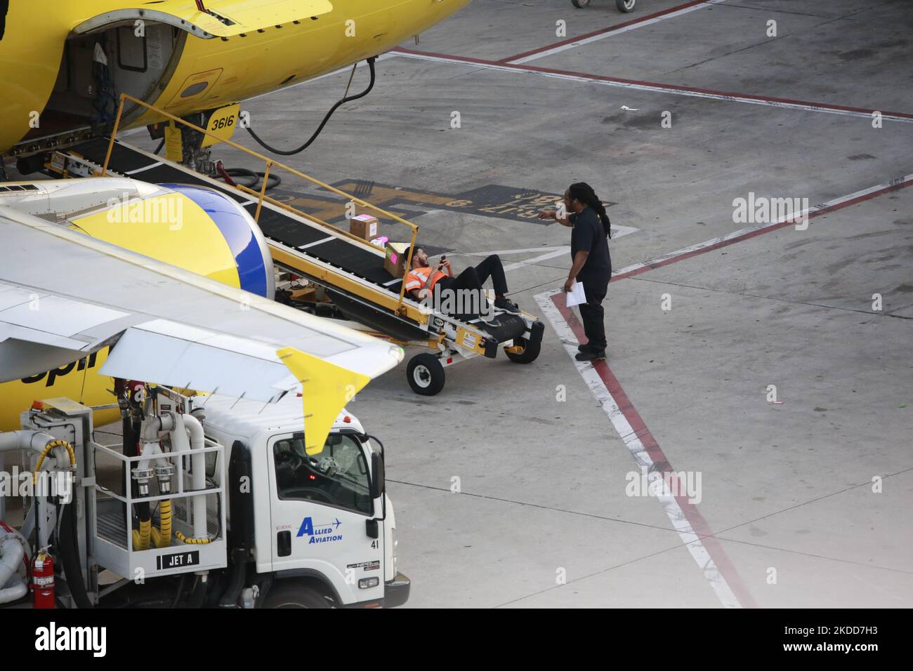 Airline workers take a break on a Spirit Airlines baggage belt at ...