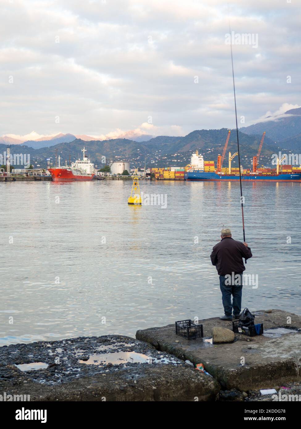Fisherman on a concrete pier. A fisherman in the port catches fish ...