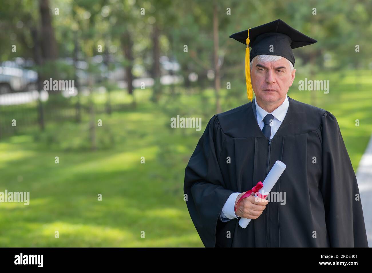 Serious old man in graduation gown holding diploma outdoors Stock Photo ...