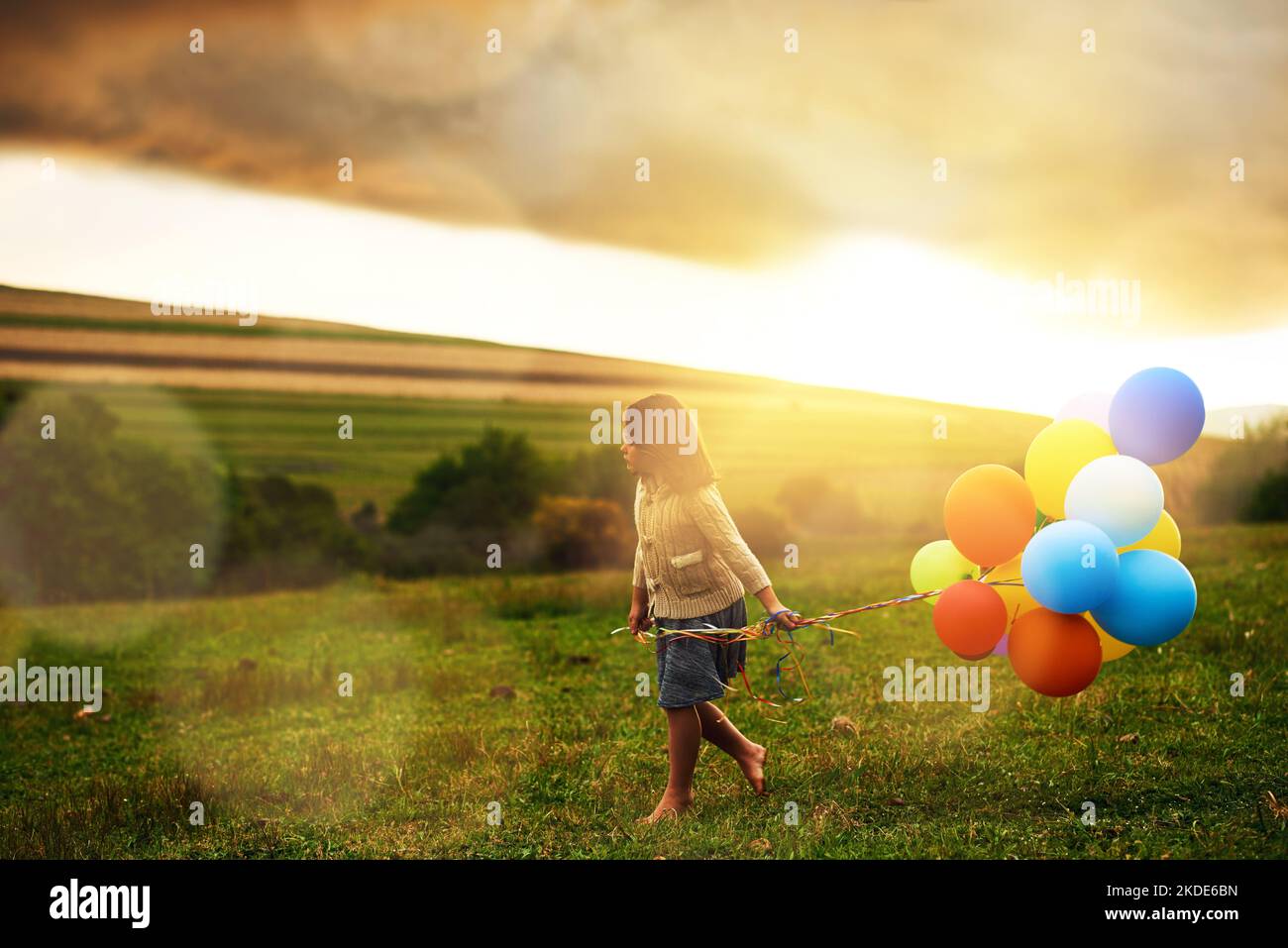 Taking her balloons for a walk. a playful little girl walking through a ...