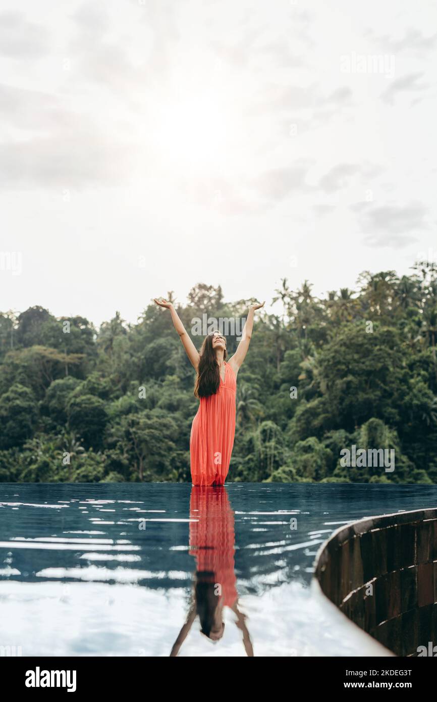 Shot of beautiful young woman standing in infinity pool with her hands ...