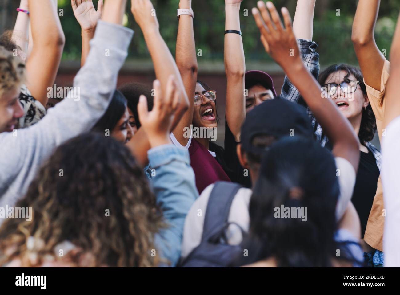 Happy young people cheering with their arms raised at a school event ...