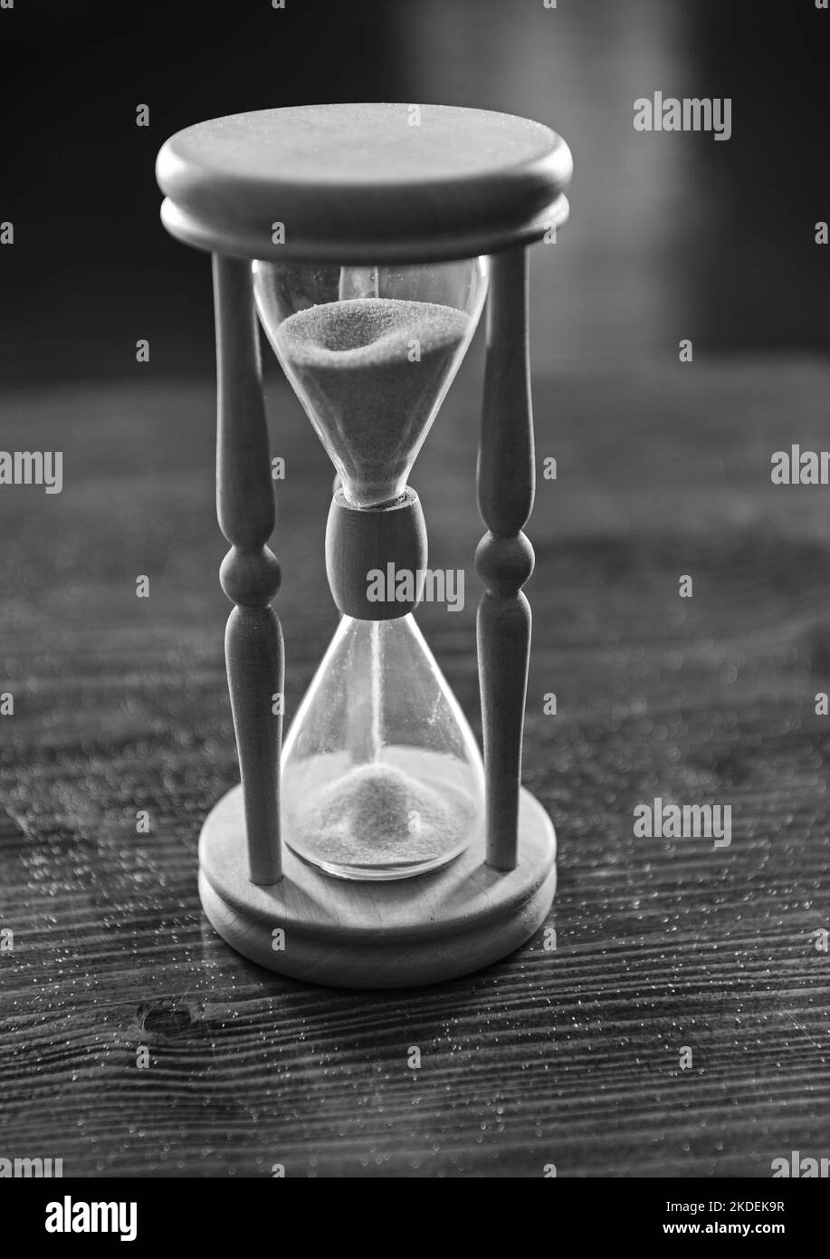 Hourglass on wooden table, dark background. Sand falling down inside of ...