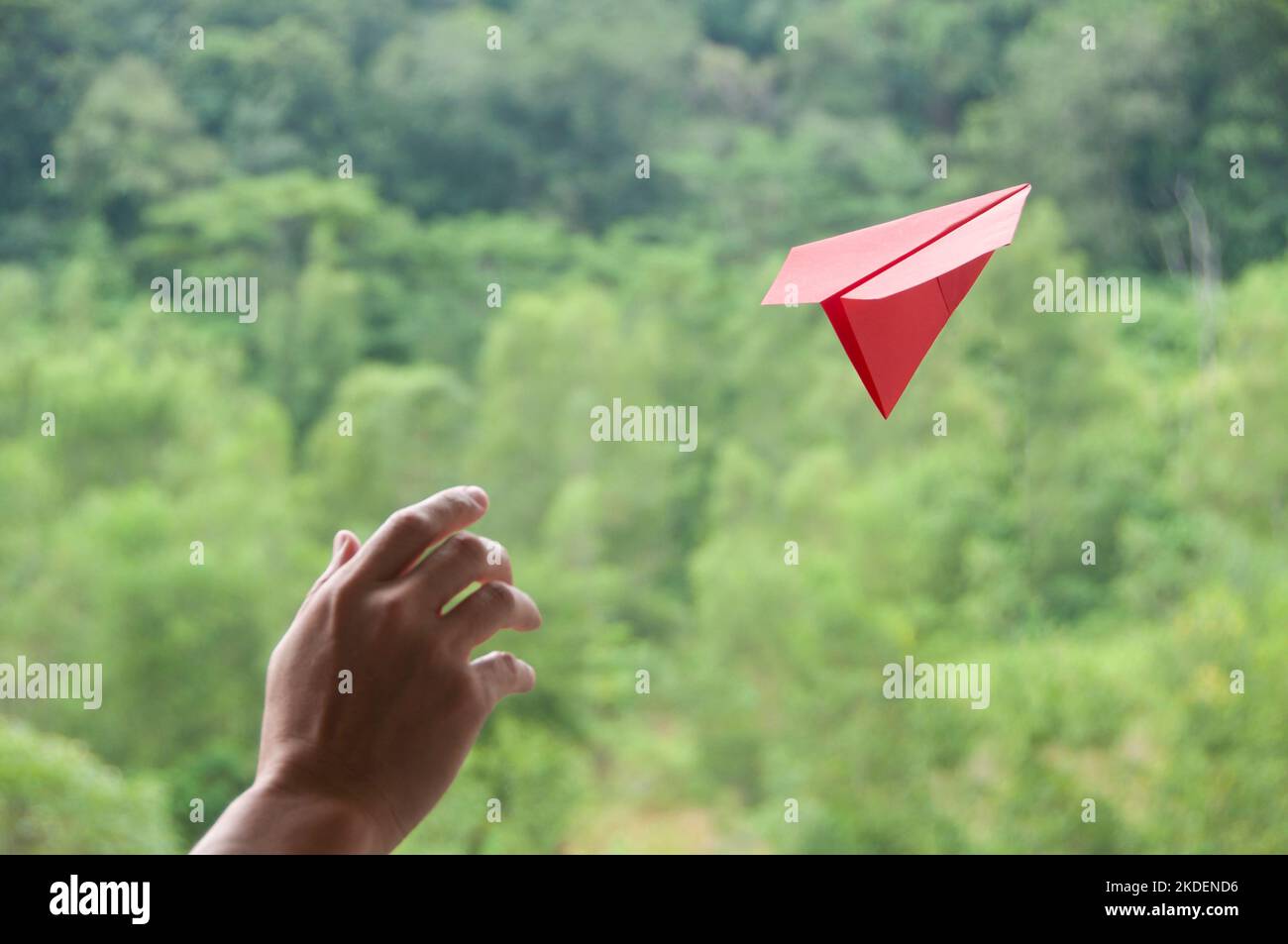 Hand throwing red paper plane with green nature background Stock Photo ...