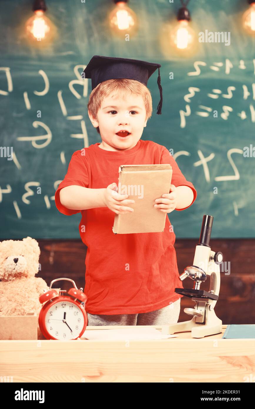 Child, pupil on cheerful face near microscope. Kid boy in graduate cap ...