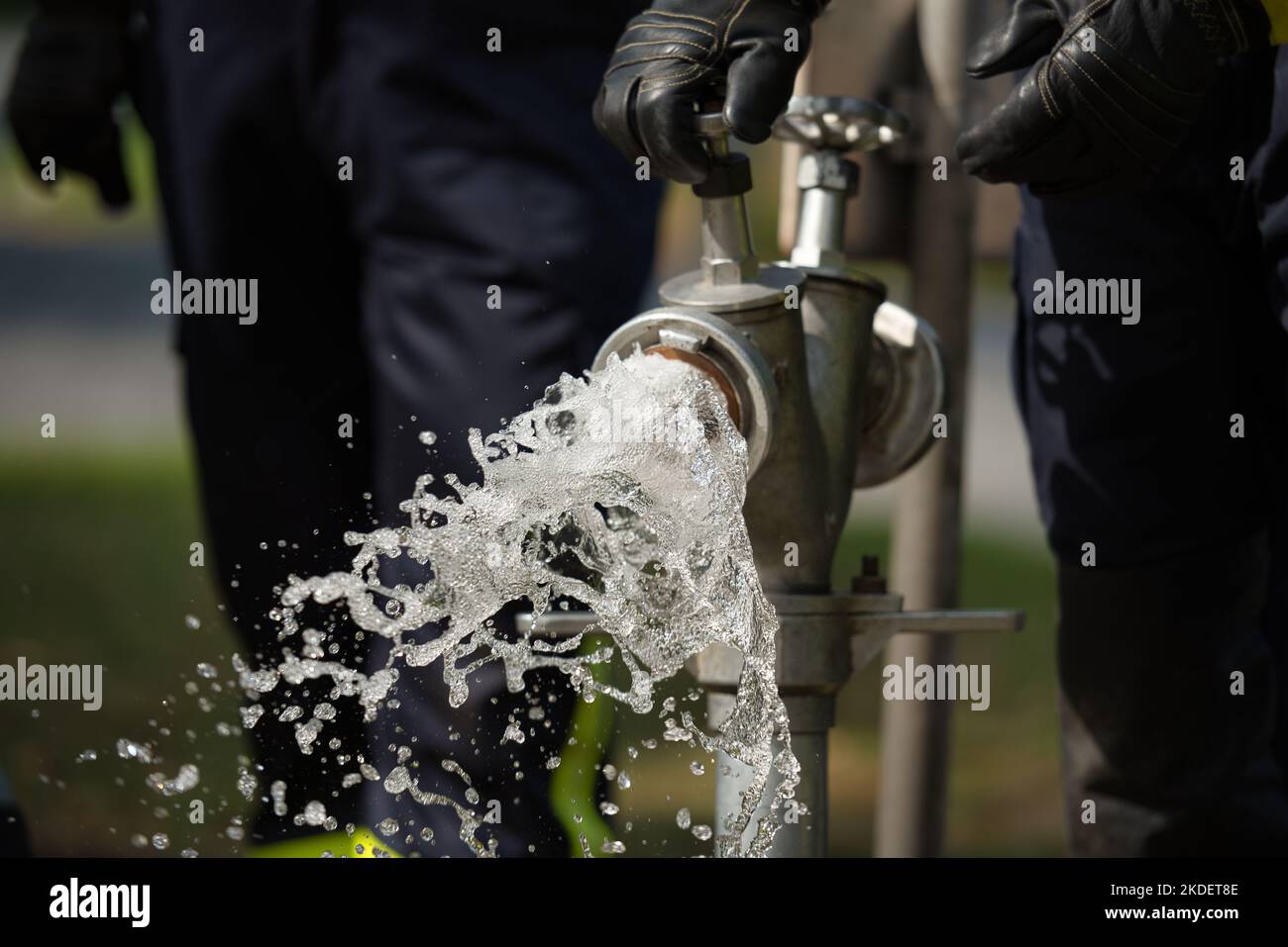 A firefighter wearing protective gloves lets water flow from a hydrant ...