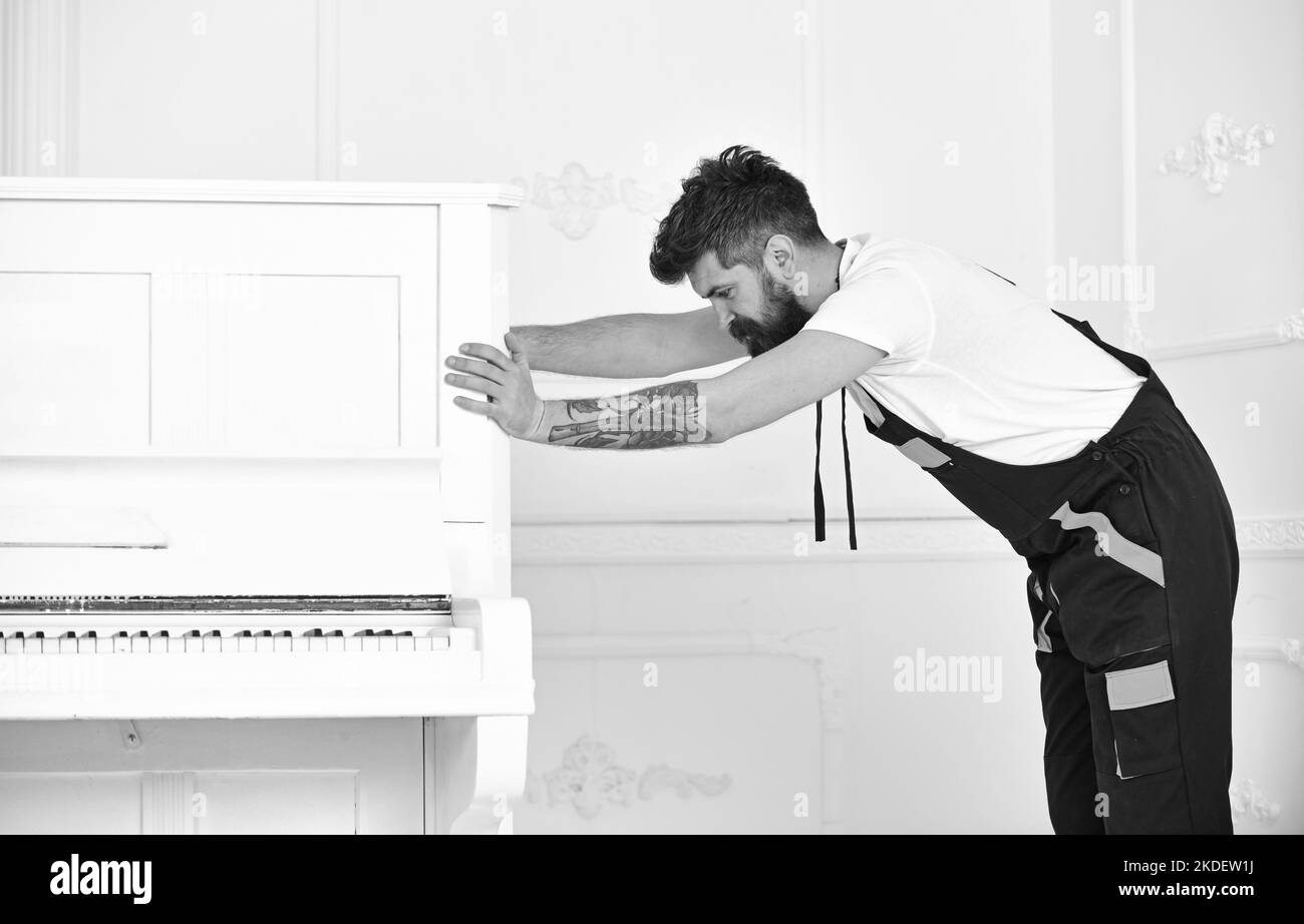Man with beard and mustache, worker in overalls pushes piano, white ...