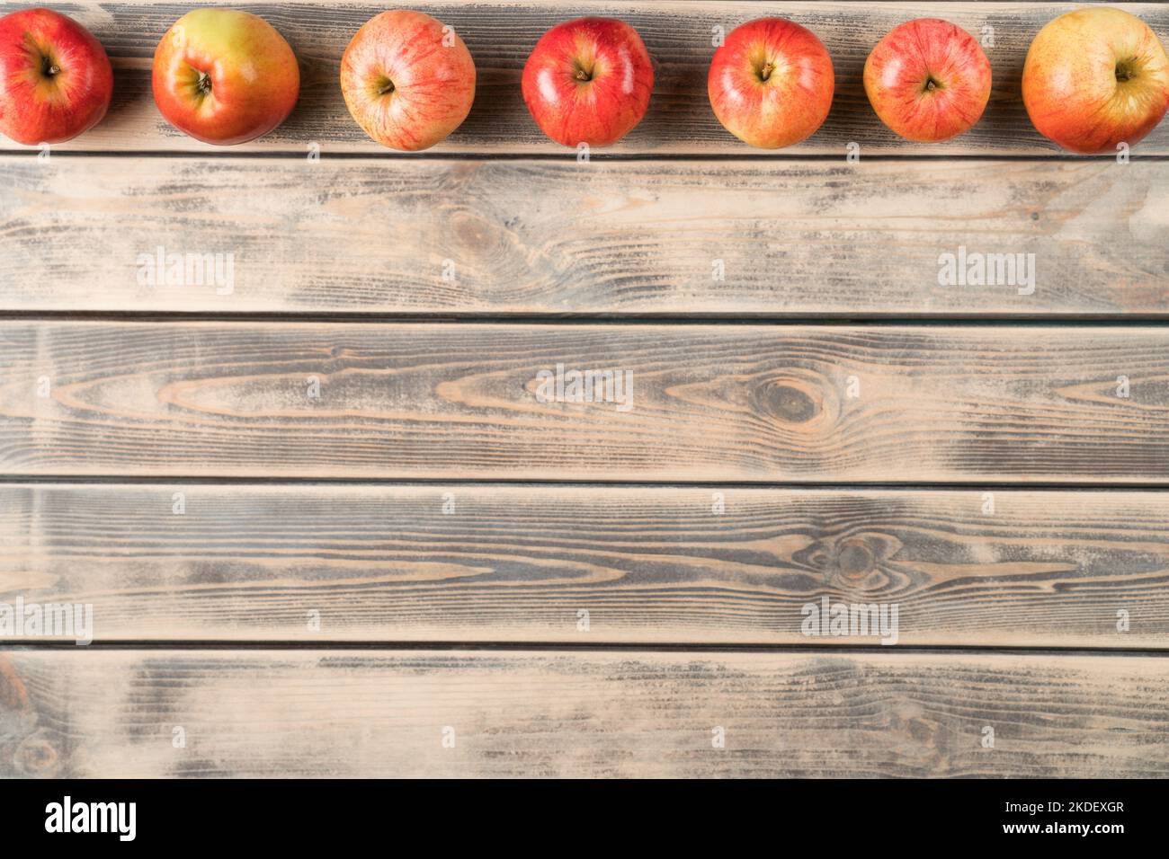 Horizontal line of fragrant sweet red apples on faded wooden table, top ...