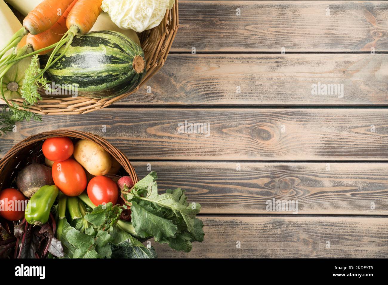 Two wicker baskets with different fresh farm vegetables on gray wooden table, top view. Bowls ...