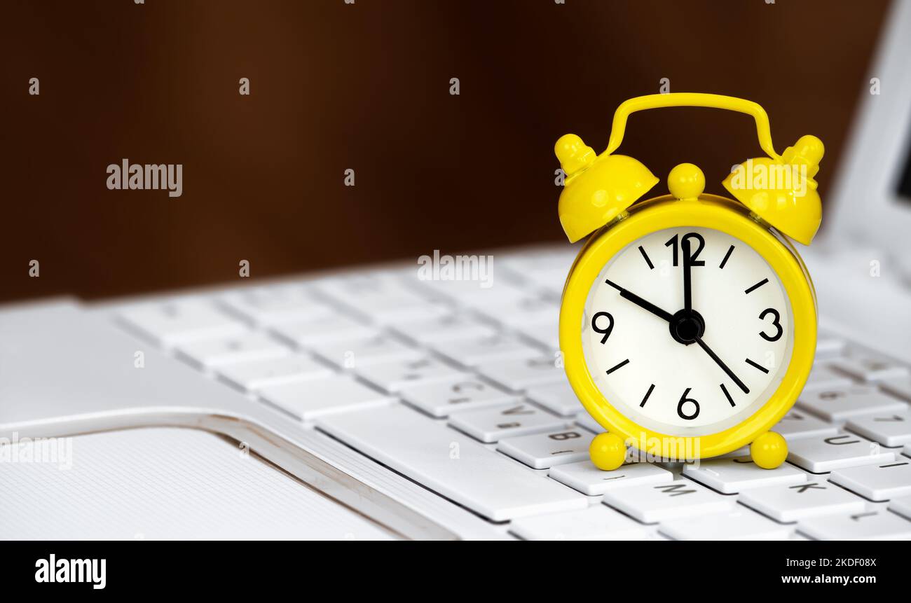 Yellow alarm clock on a white laptop. Daylight savings time banner or ...