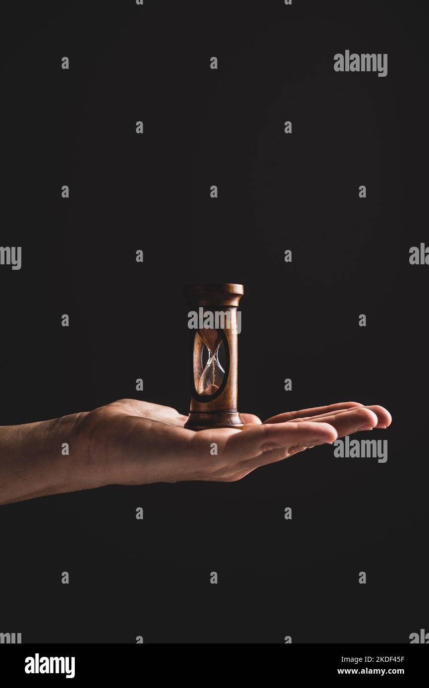 A female hand holding hourglass on black background Stock Photo - Alamy
