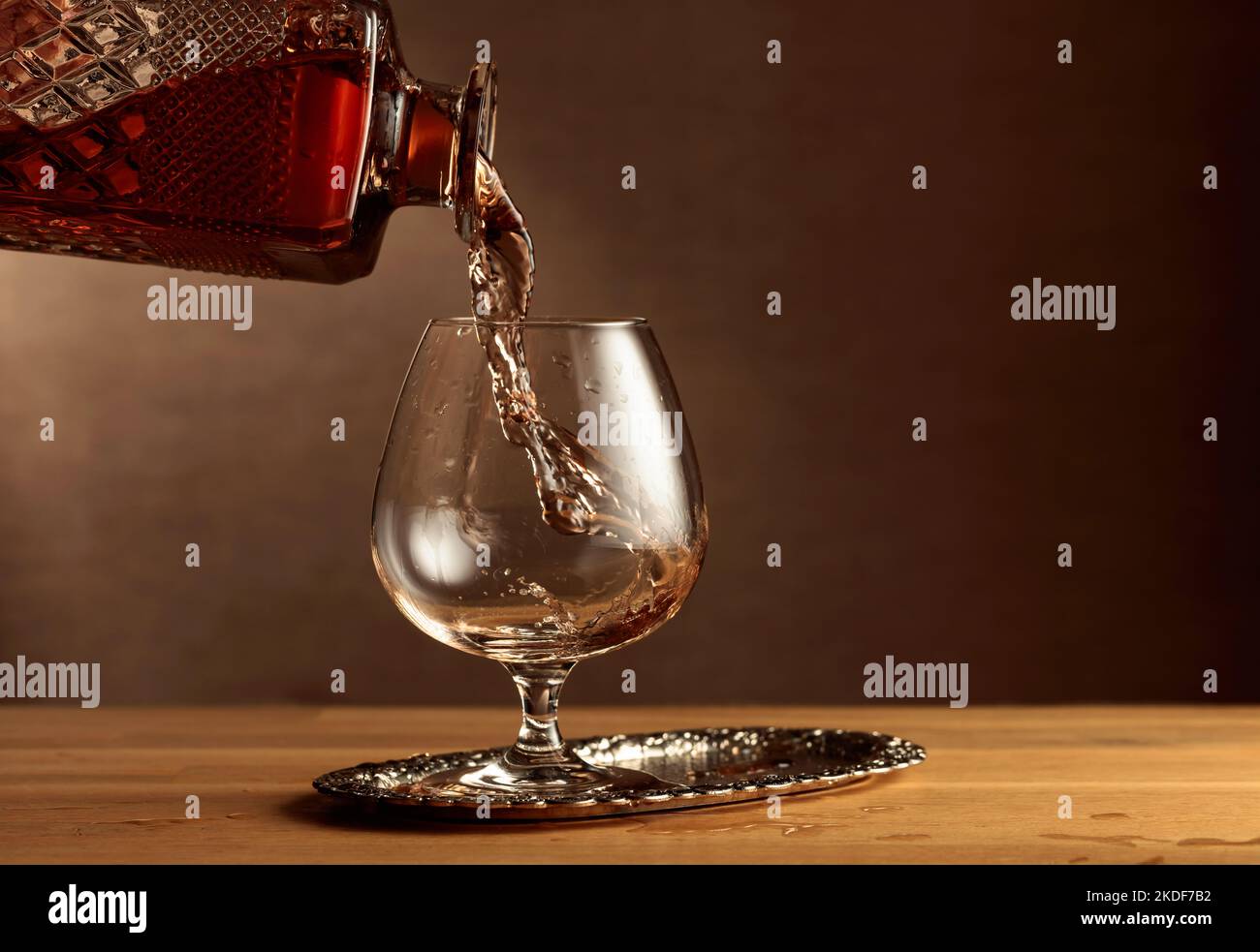 Brandy is poured from a decanter into a snifter glass. Cognac on an oak ...