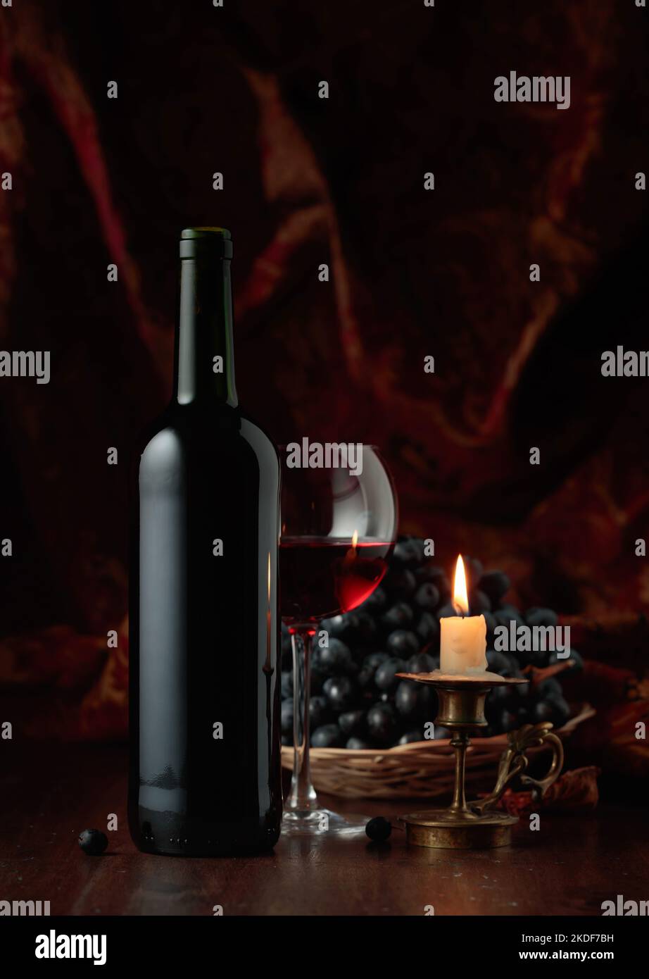 Still life with red wine, grapes, and a burning candle in an old brass ...