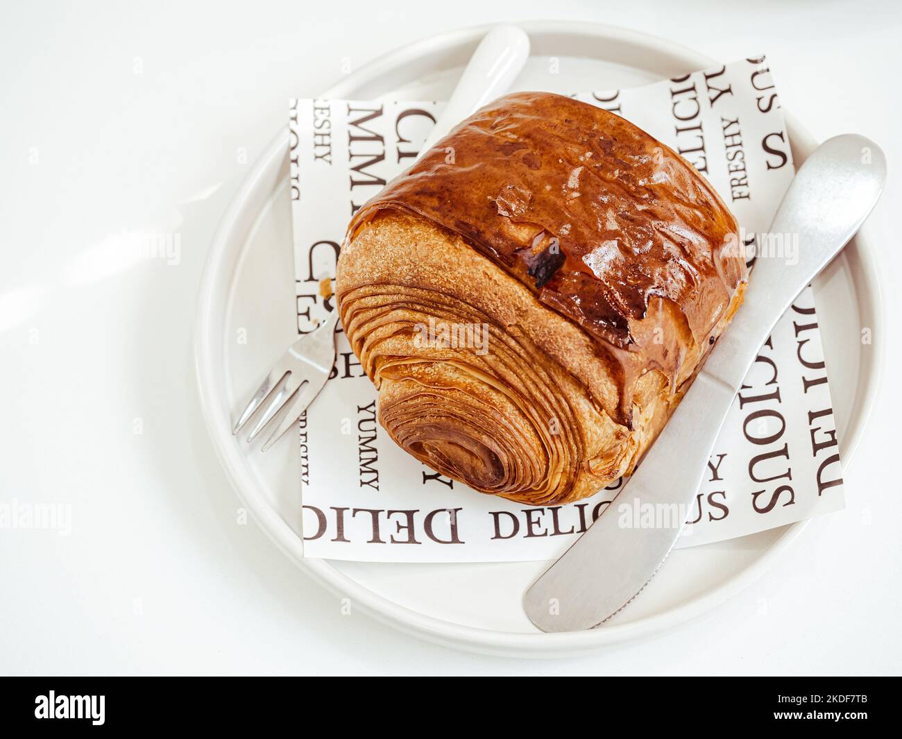 French croissant with metal knife and fork on paper on white round ...