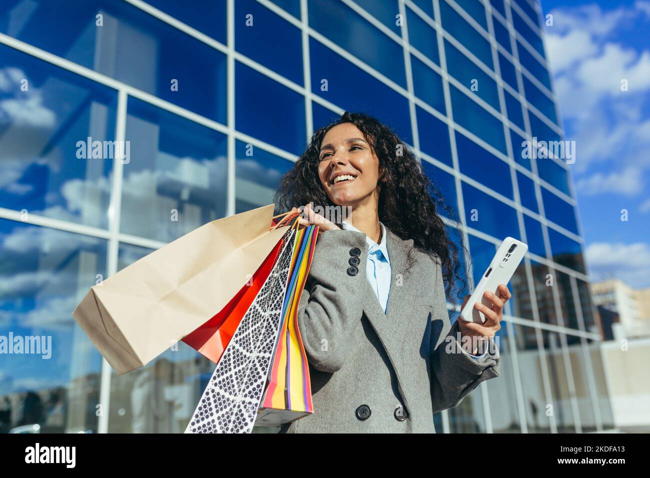 Happy woman shopper outside near big mall store, holding smartphone and ...