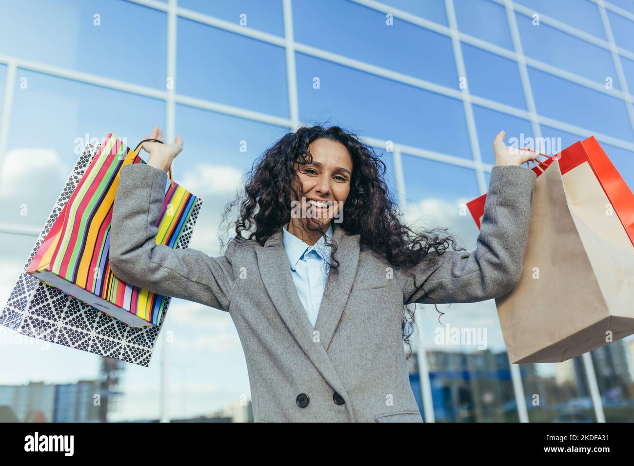 Beautiful woman with curly hair outside big store looking at camera and ...