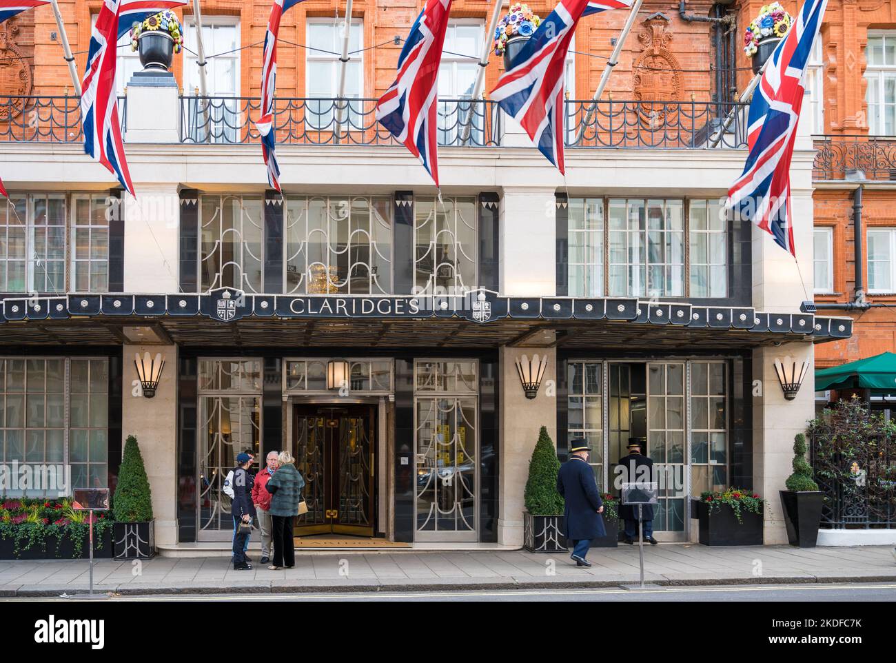 Group of four people stand in conversation outside the main entrance to Claridge's Hotel on ...