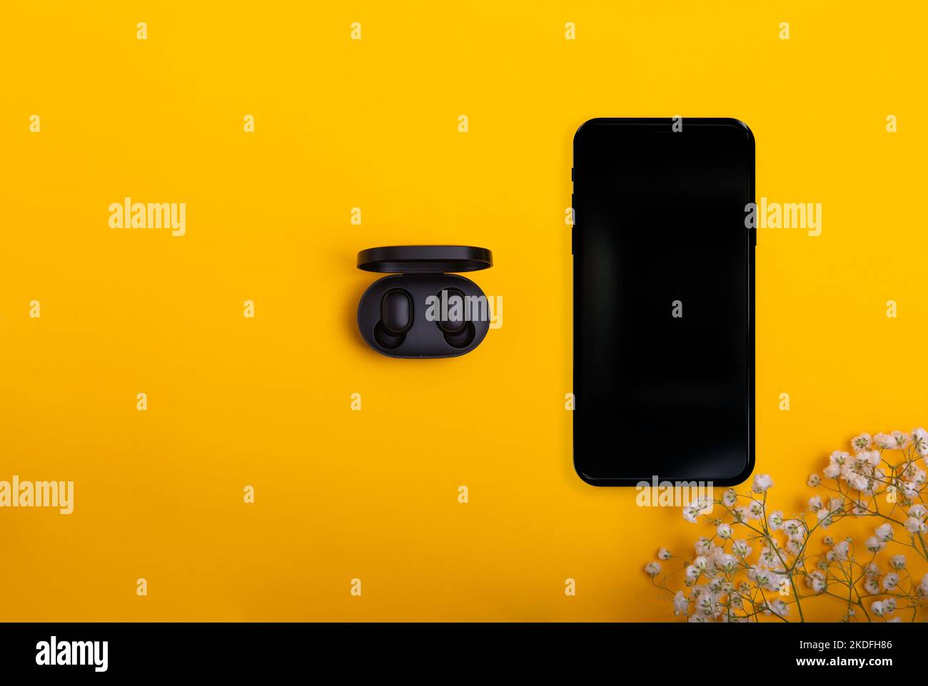 A black smartphone and black wireless earphones isolated on a yellow ...