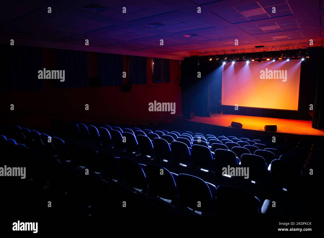 A large empty conference hall with blue empty seats, illuminated lights ...
