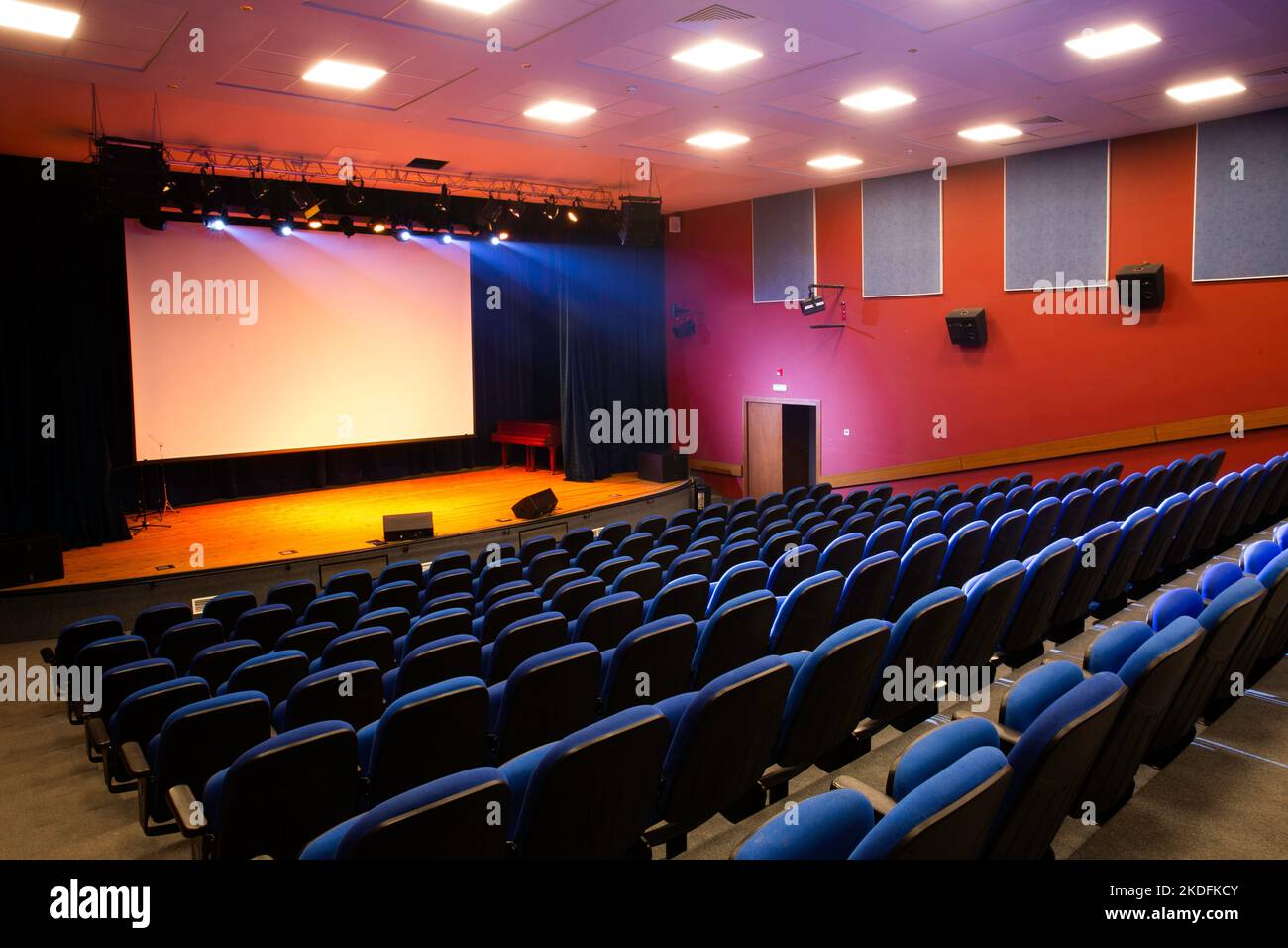 A large empty conference hall with blue empty seats, illuminated lights ...
