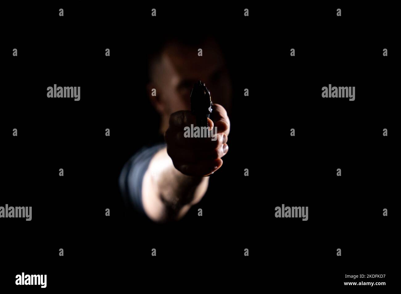 A man in a dark shallow focus pointing a gun to the camera Stock Photo ...