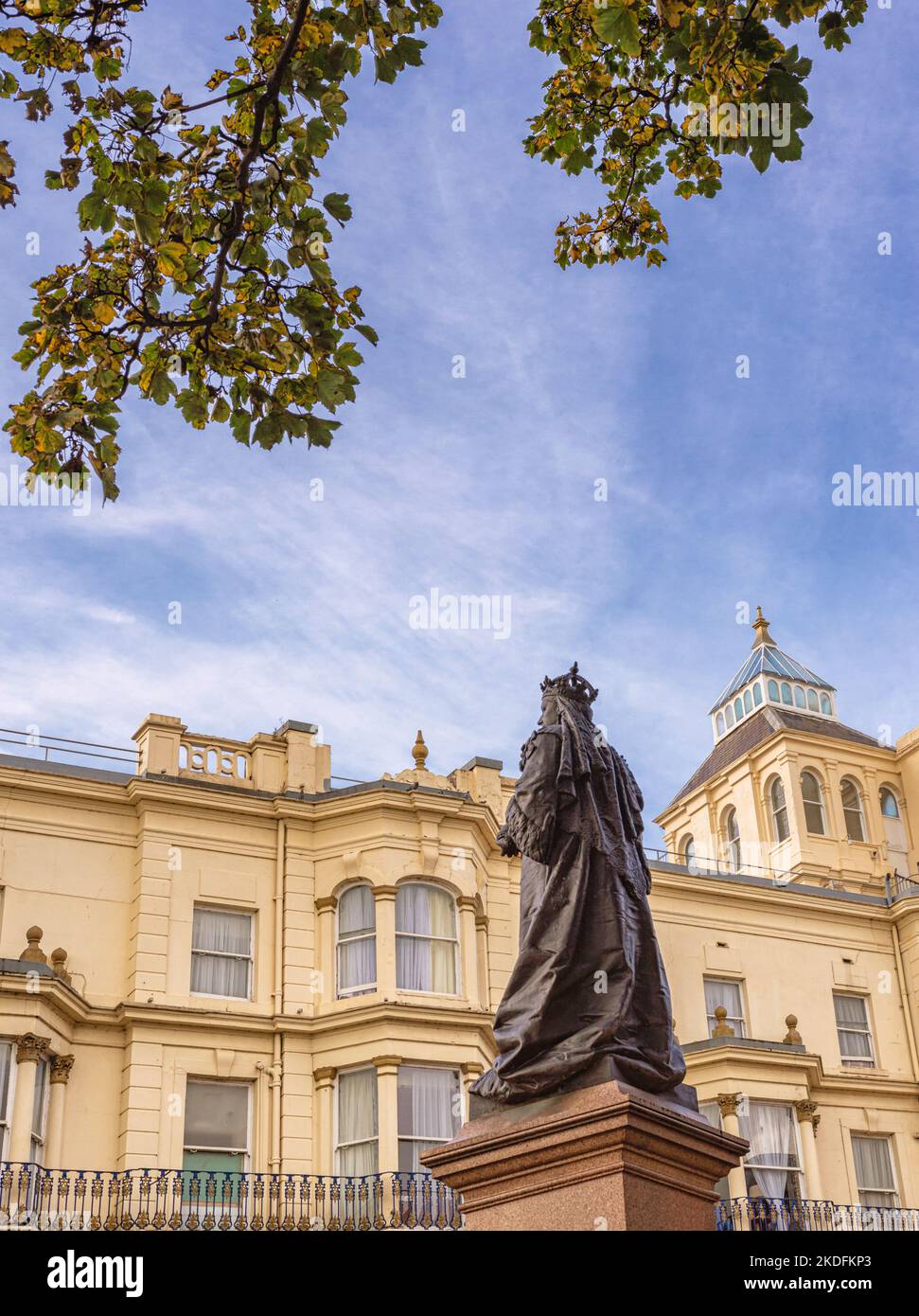 A statue of Queen Victoria overlooks a stone building with a tower ...