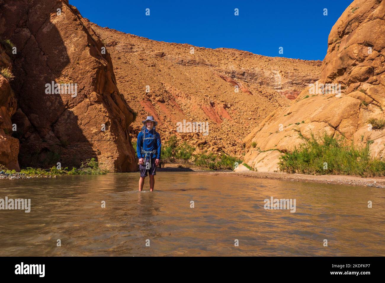 Young male trekker in The Valley of the Roses wading through the M'Goun ...