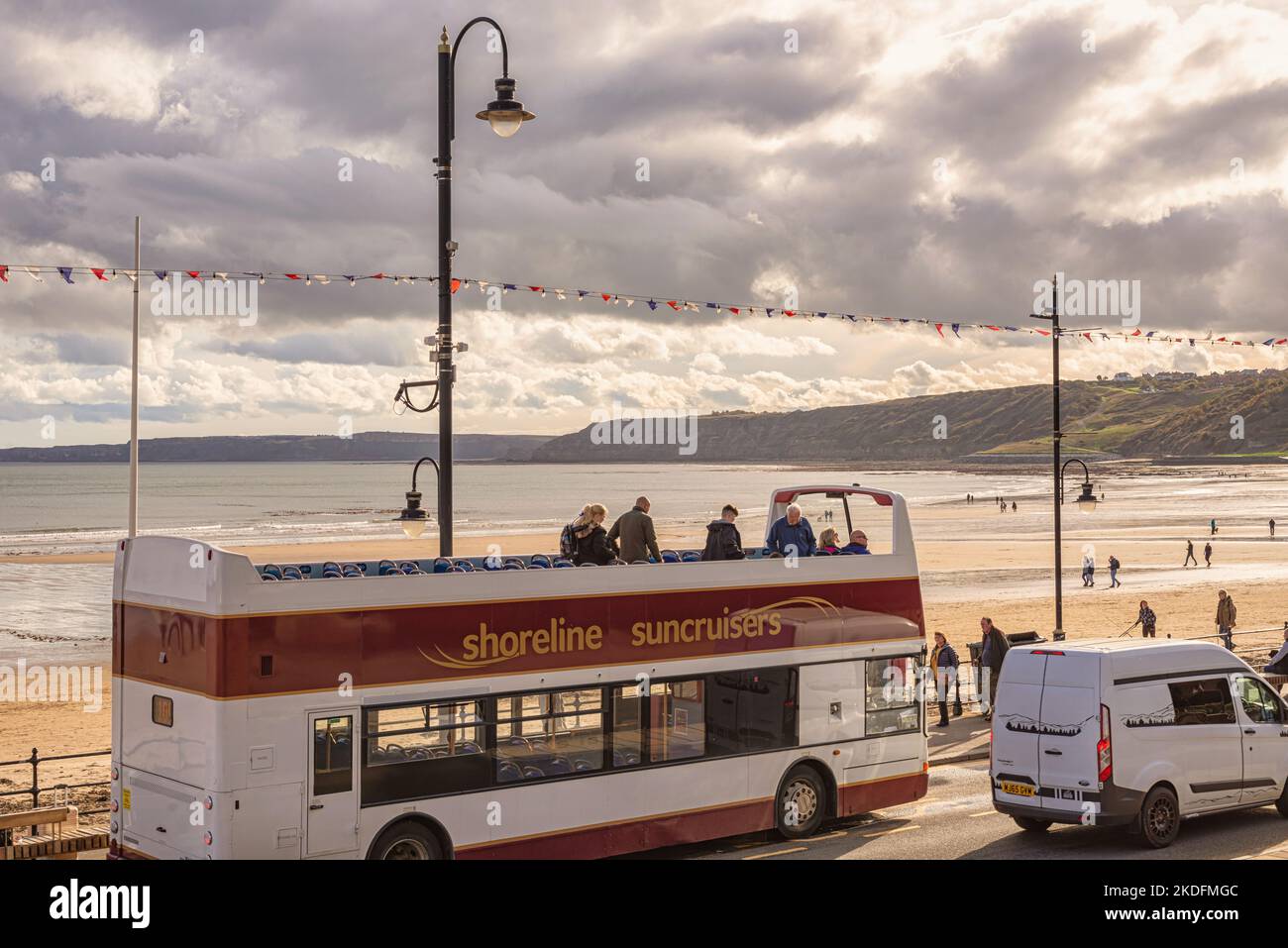 A tourist bus is parked on a promenade at the seaside. People are ...