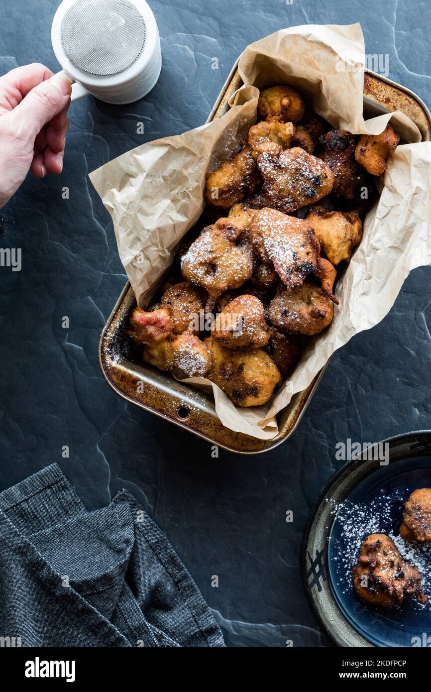 A loaf pan filled with fritters and a hand holding a container of icing ...