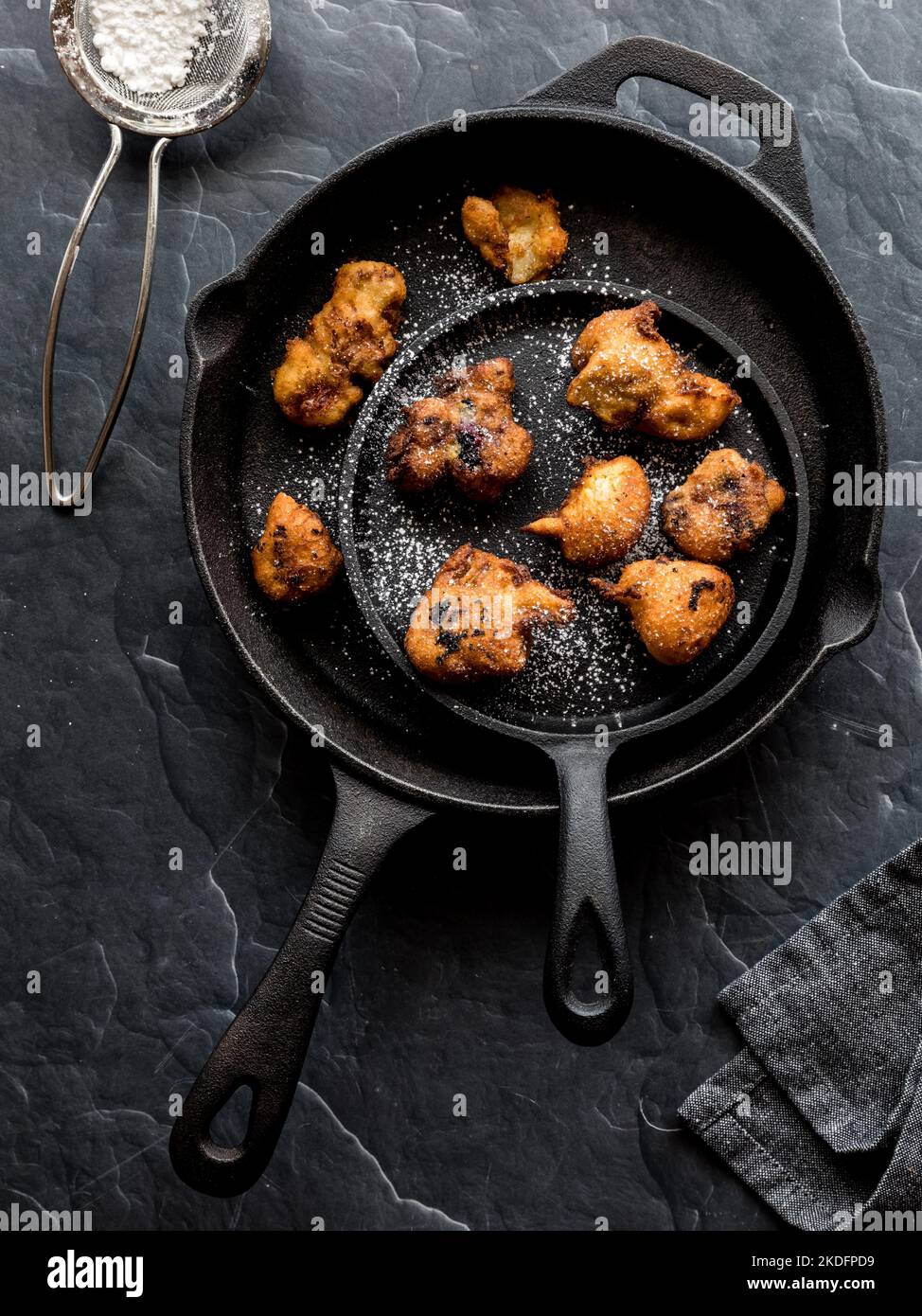 Top down view of fritters with powdered sugar in cast iron fry pans ...