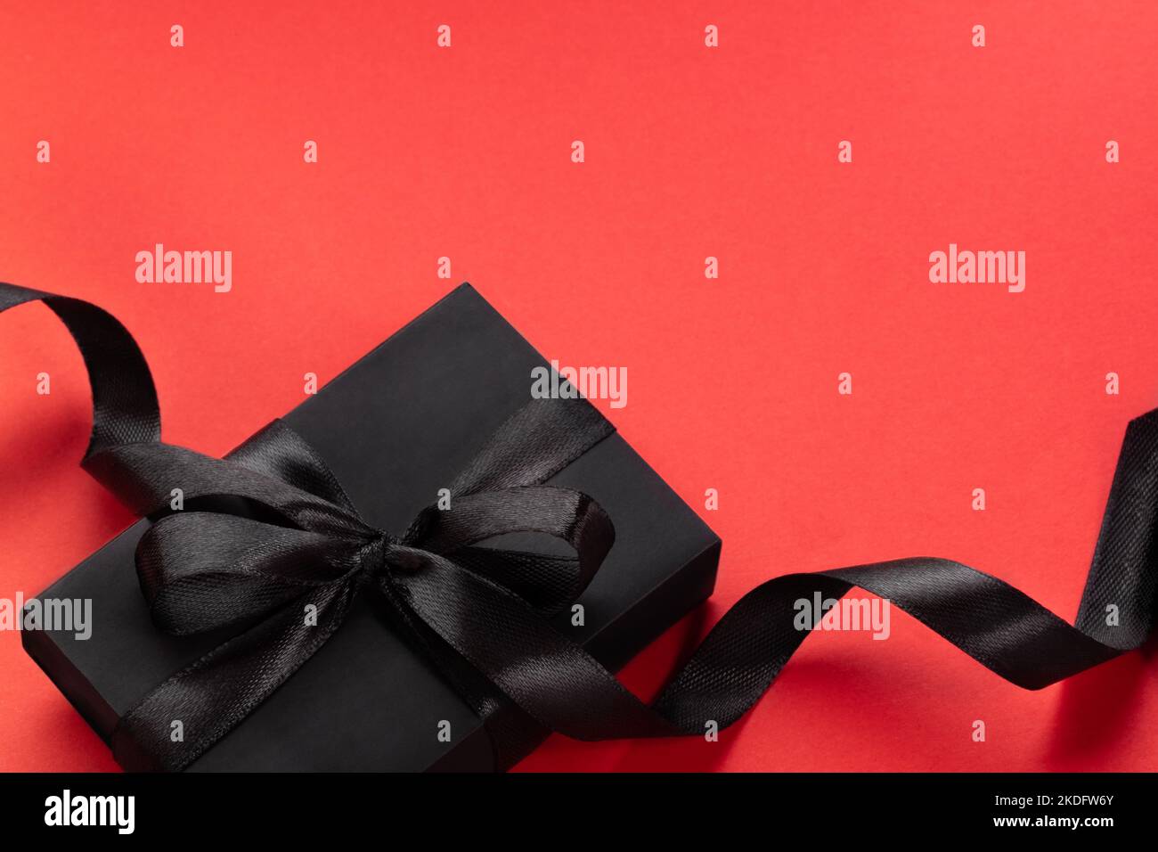 Black wrapped gift box with black ribbon and bow on red. Minimal ...